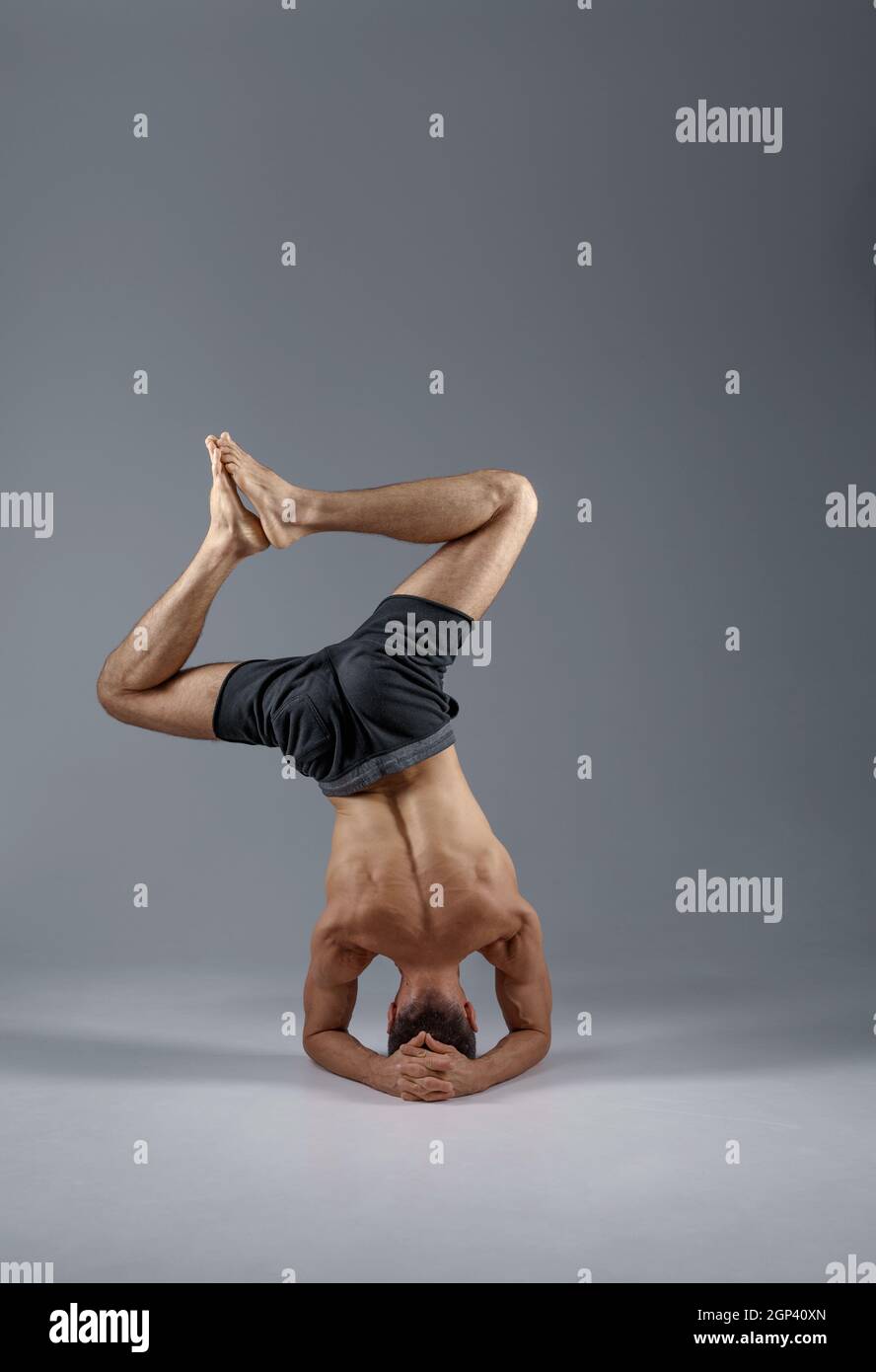 Male yoga standing on his head and elbows, back view, meditation, grey ...