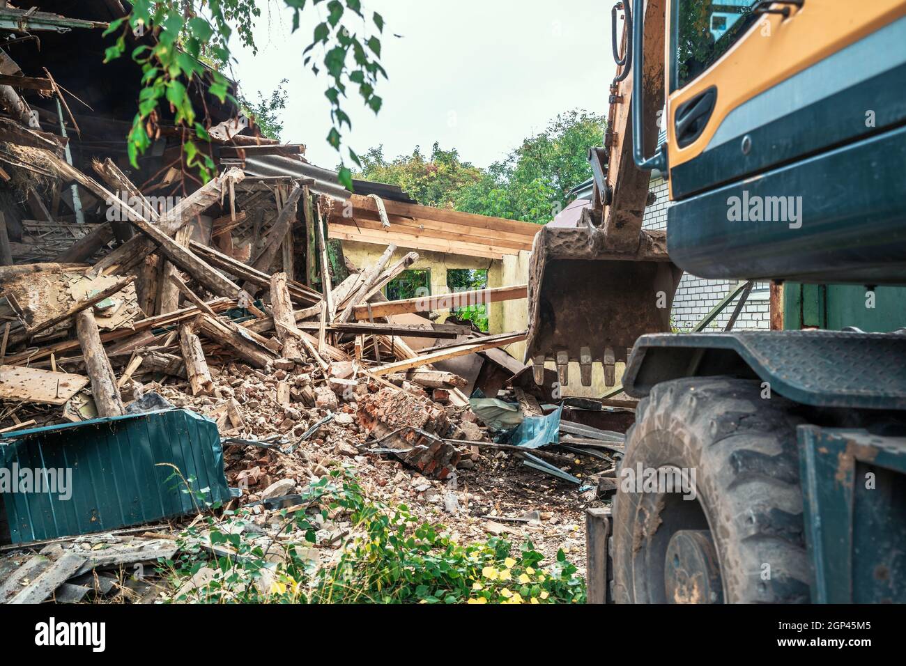 Demolition of house. Broken walls of old building and excavator at site ...
