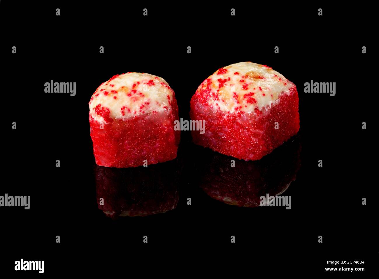 Two red tuna rolls with red caviar and shrimp on a black background ...