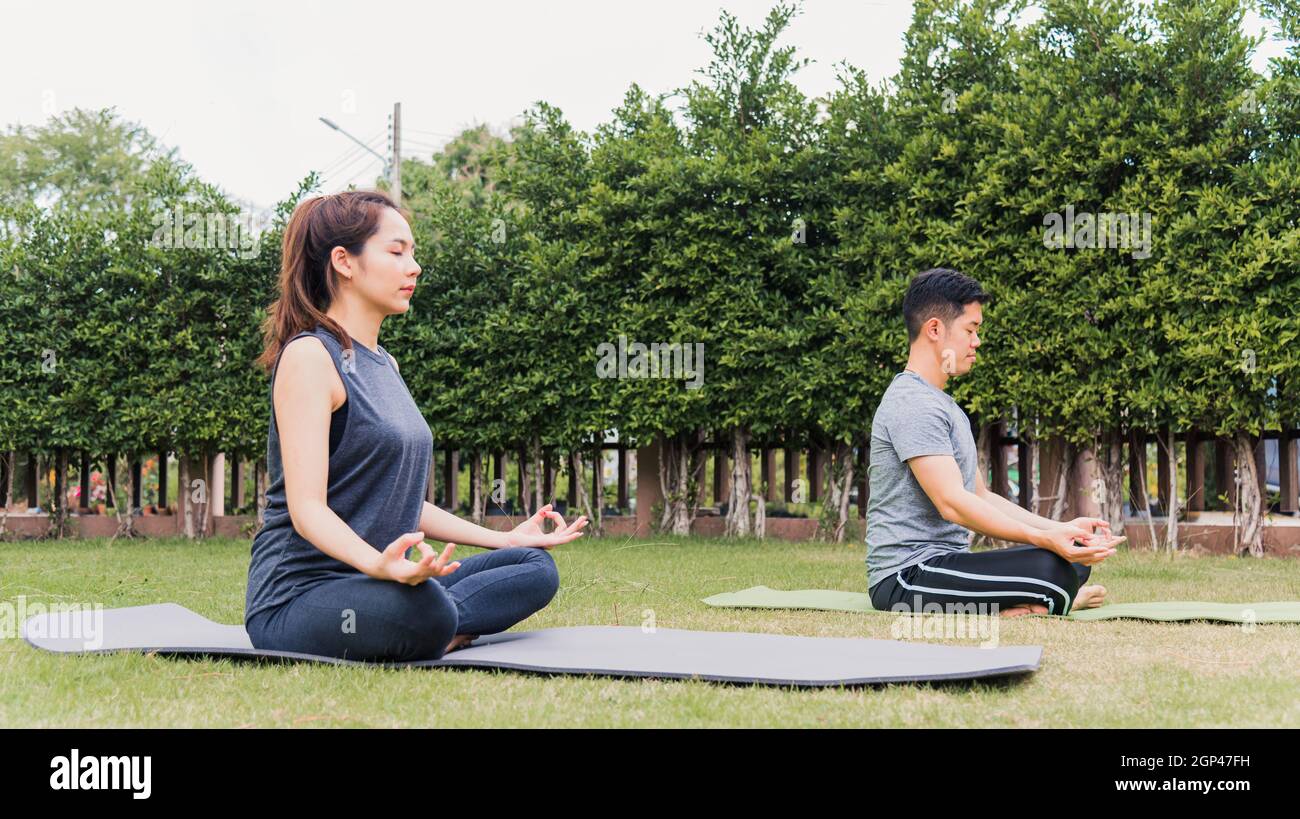 Asian man and woman practicing doing yoga outdoors in meditate pose ...
