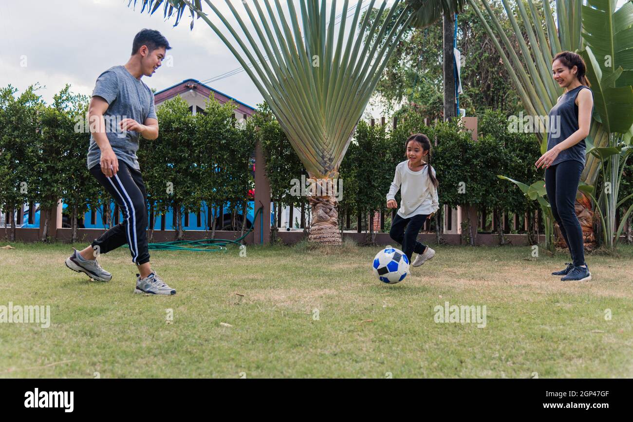 Asian young mother, father and child daughter playing soccer outside in ...