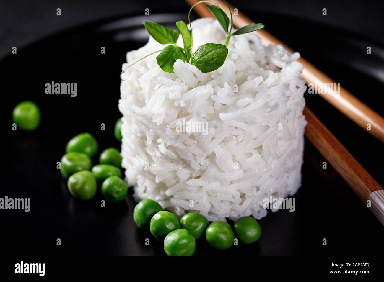 Garnish of white long rice with green peas and green sprouts on a dark ...