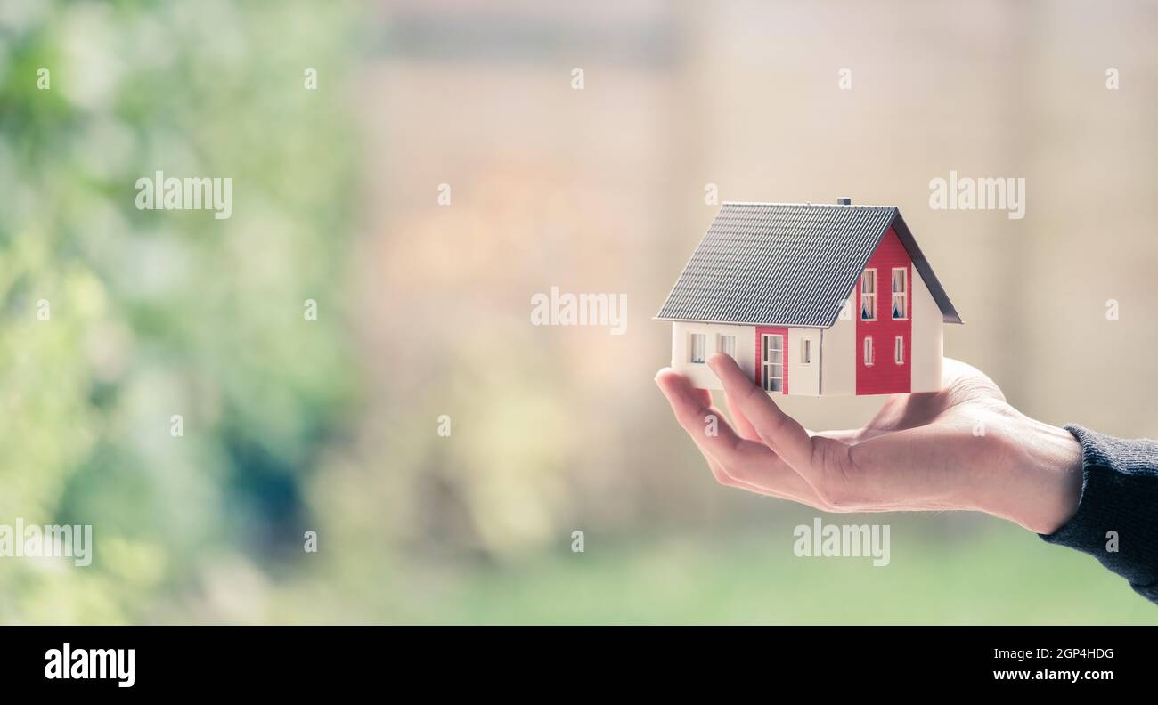 New home and house concept: Red house model outdoors in male hand, copy ...