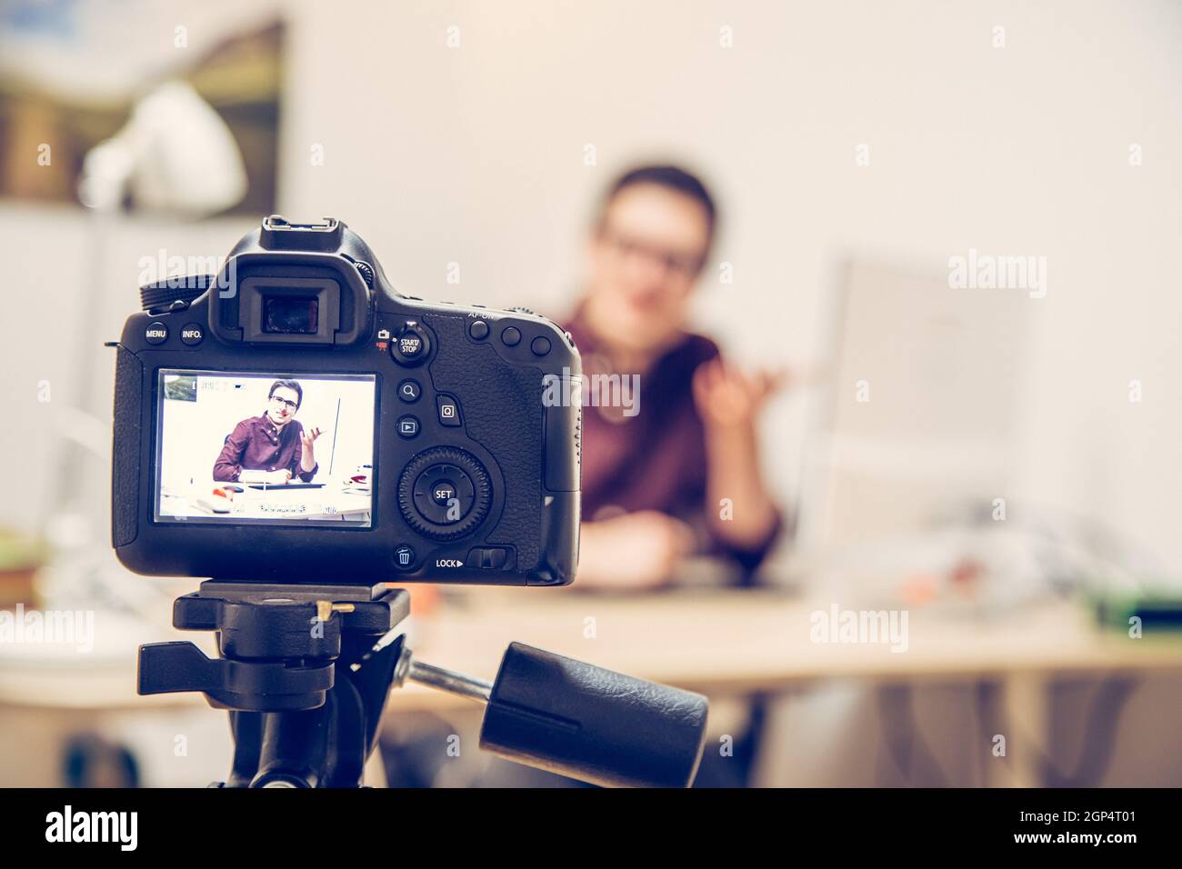 Camera on a tripod filming a blogger at home sitting on his workspace ...