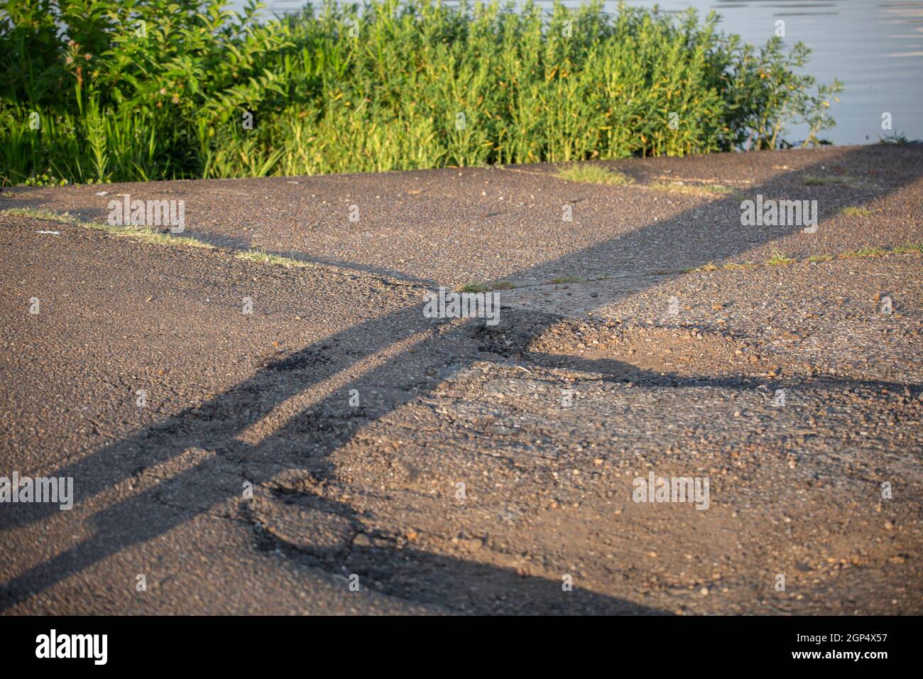 Human shadow stretching toward the corner of asphalt where green space ...