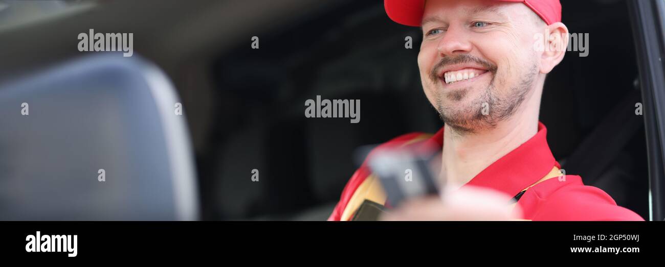 Portrait of young smiling courier driver in car window with box in hand ...