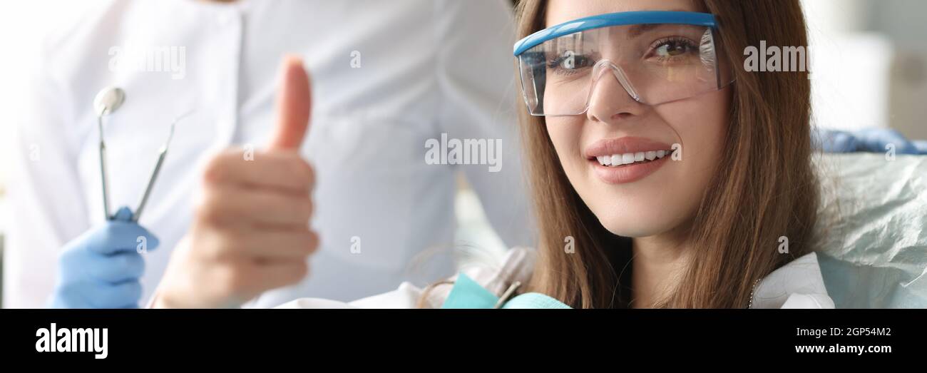 Portrait of woman with a beautiful smile at dentist showing thumbs up ...