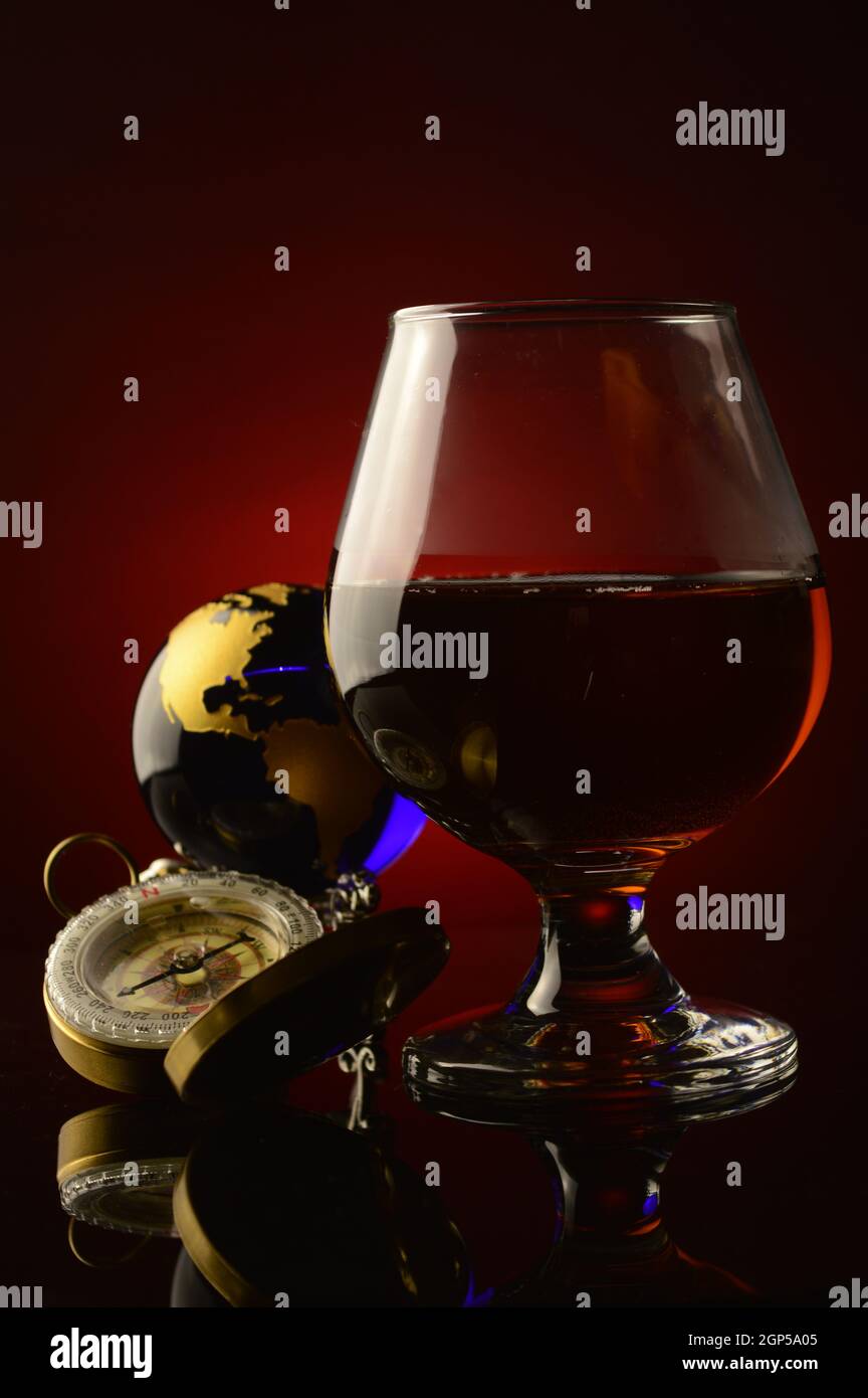 A glass of Cognac with a compass and globe over a dark red and black background Stock Photo - Alamy