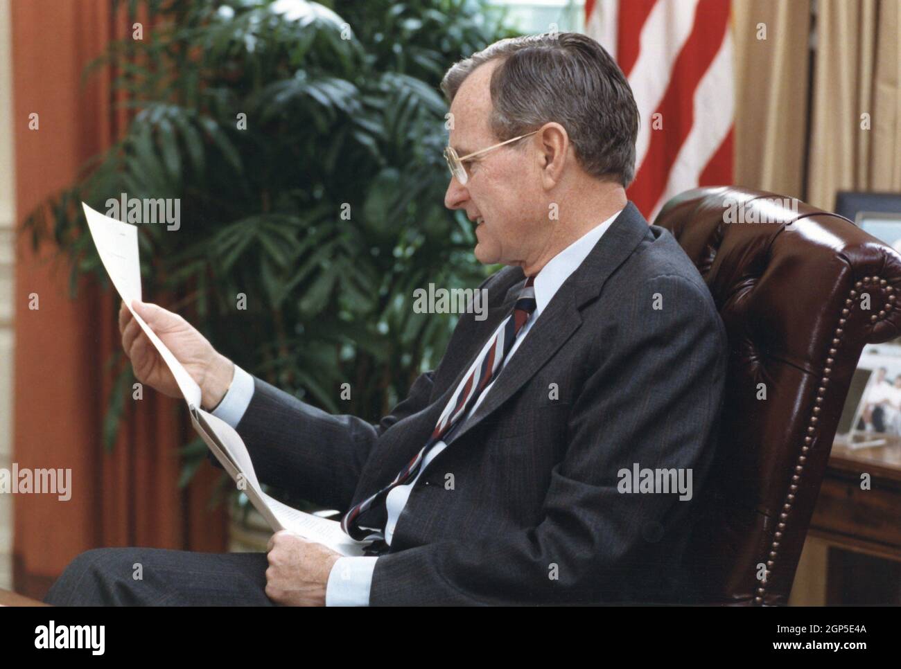 President George H.W. Bush, reading a document at his desk in the White ...