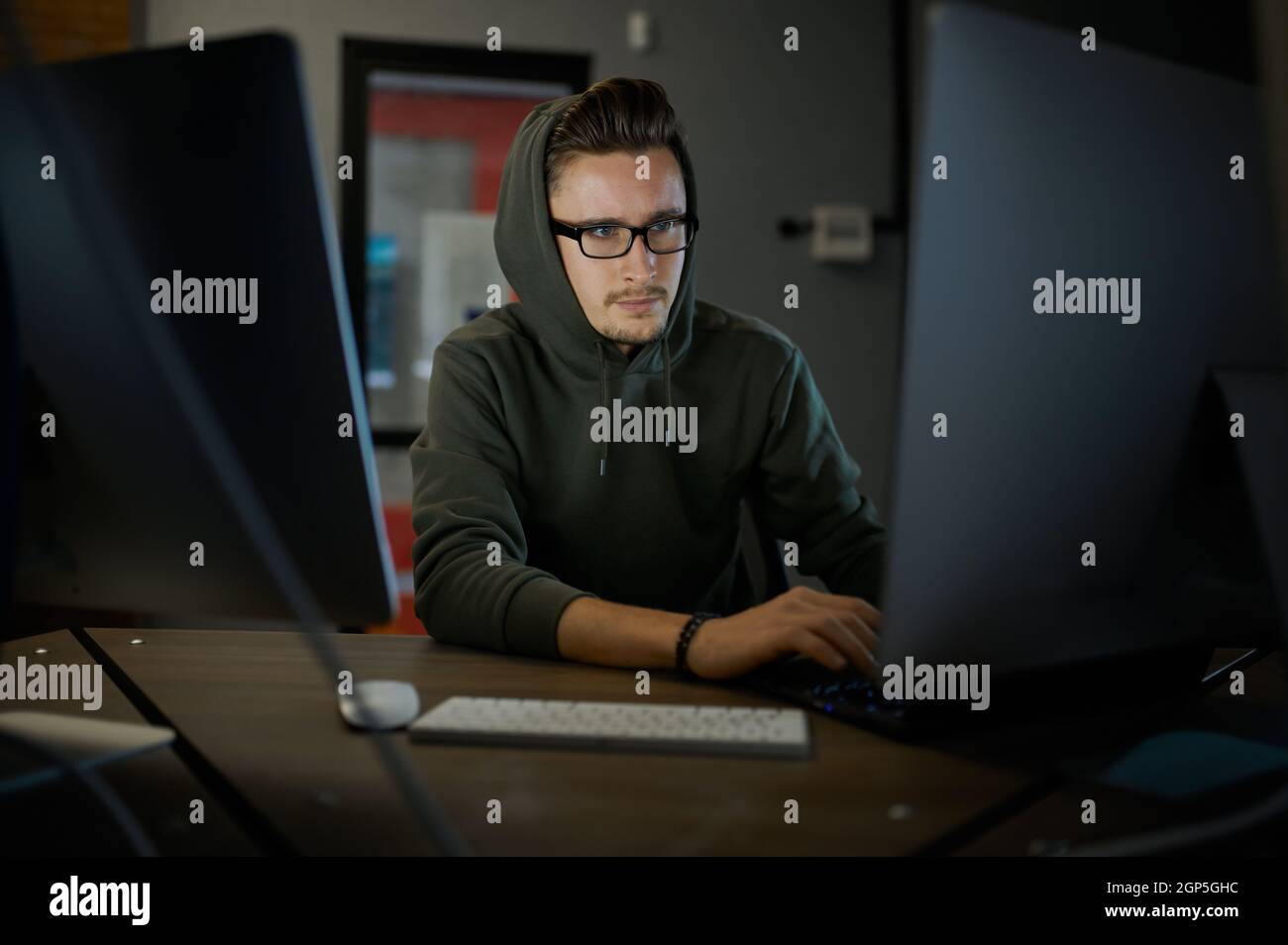 Male internet hacker in hood and glasses sitting at monitors. Illegal ...