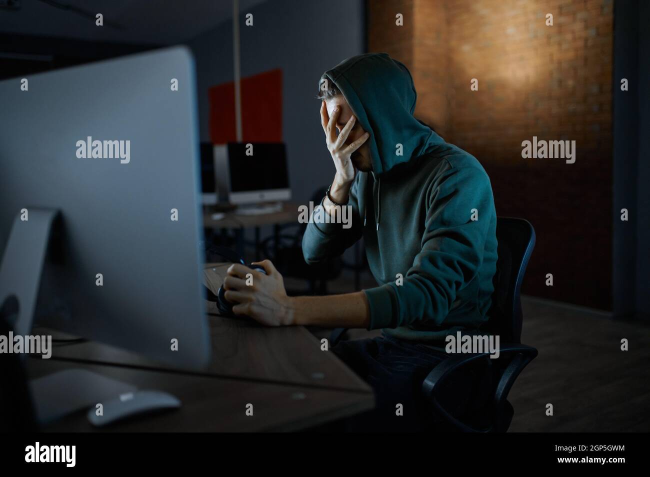 Serious male internet hacker in hood works on computer, front view ...