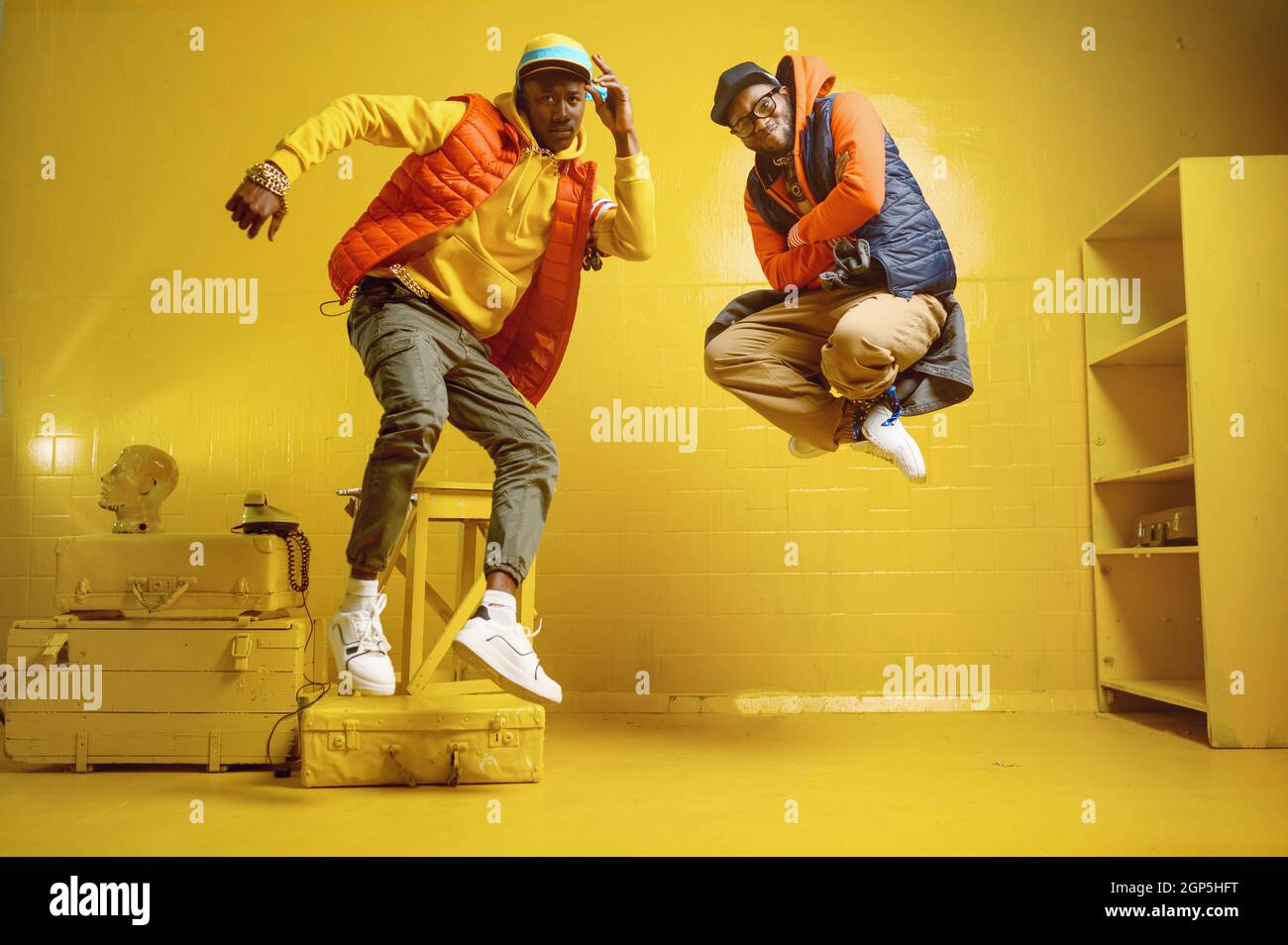 Two stylish rappers with gold jewelry in cool studio, yellow background ...