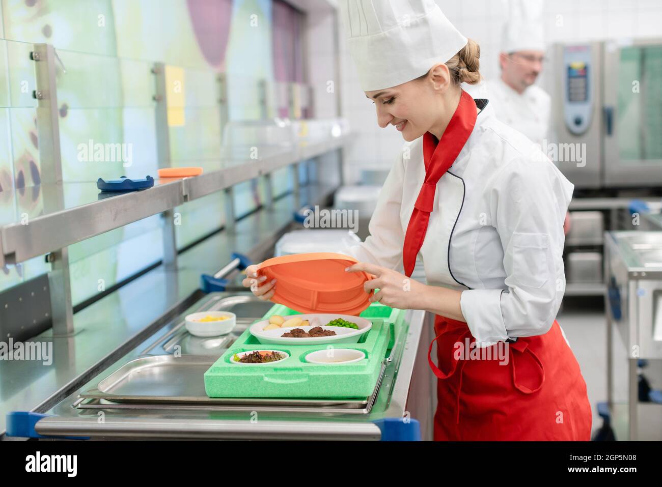 Chef in commercial kitchen preparing meal in heat retaining packaging ...