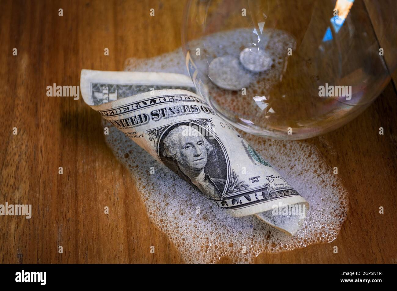 A rolled up dollar bill and coins, partially covered by foam on a ...