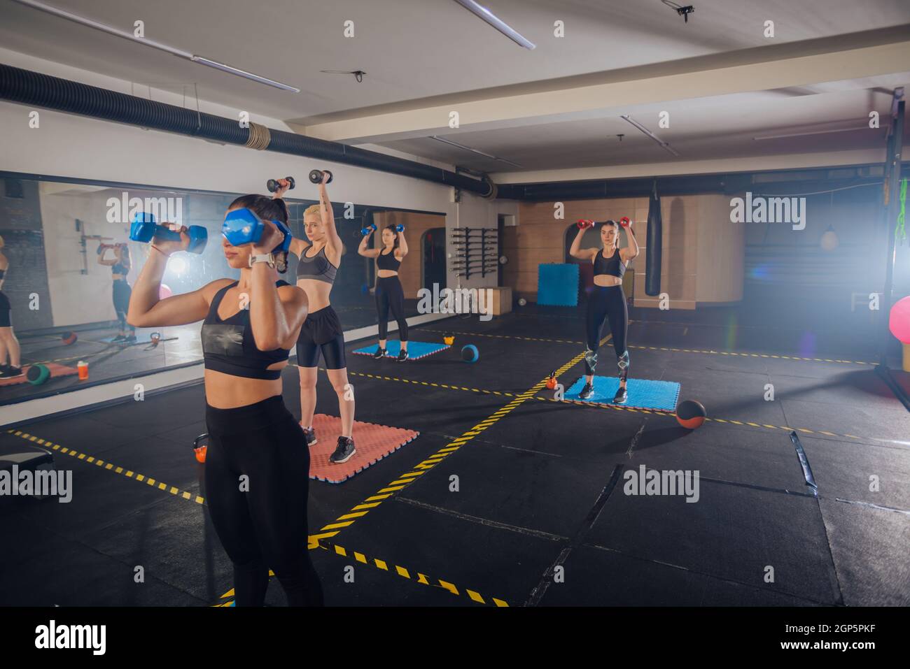 Group of athletic young women in sportswear with dumbbells exercising ...