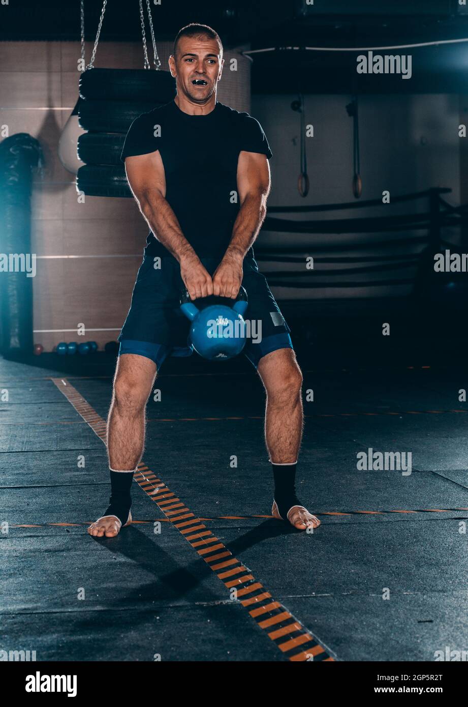 Handsome strong man doing the exercises with kettlebells on dark shadow ...