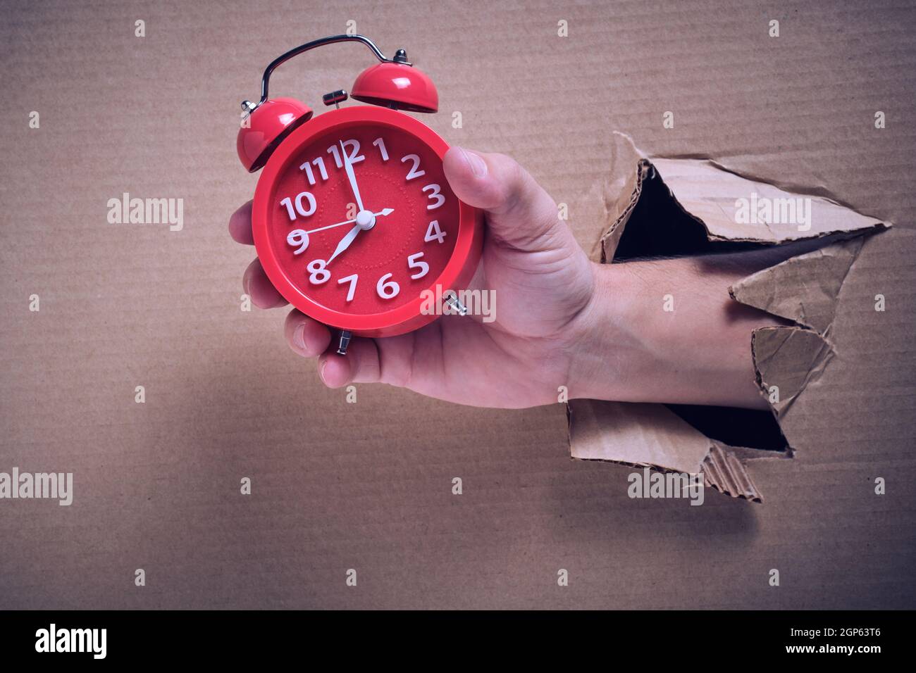 Red alarm clock in his hand, a torn cardboard wall.Eight morning or ...