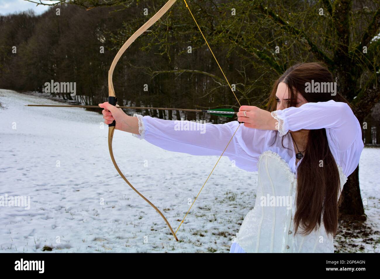 A young woman standing sideways with a bow and arrow in the snow in ...