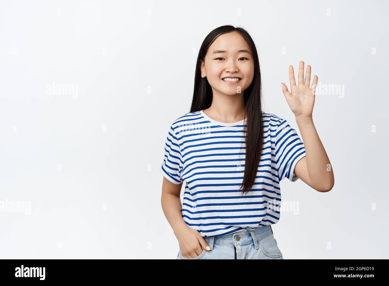 Friendly asian teen girl saying hi, waving raised hand and smiling ...