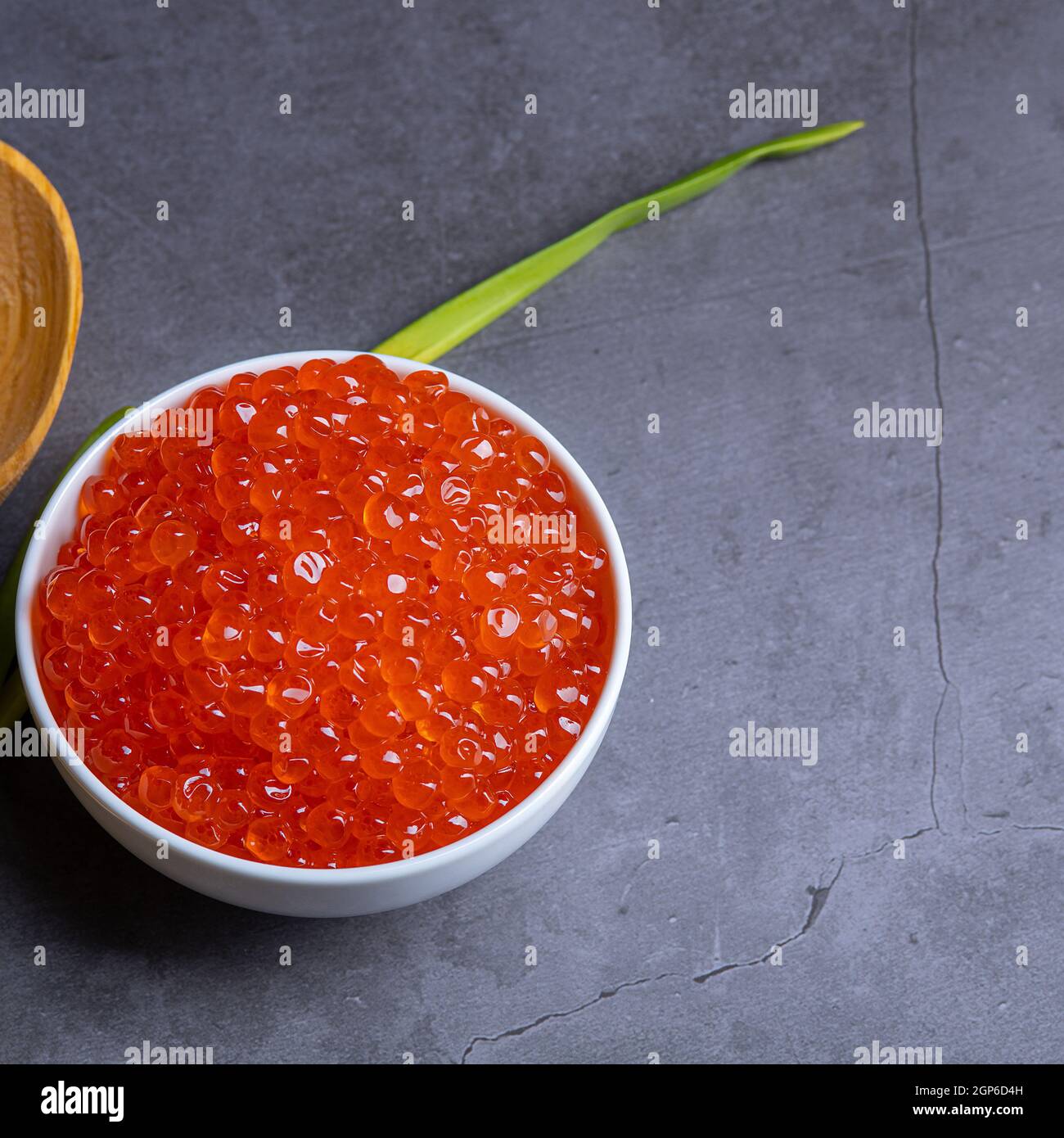 Red caviar in a wooden cup on a grey background with a spoon. Place for ...