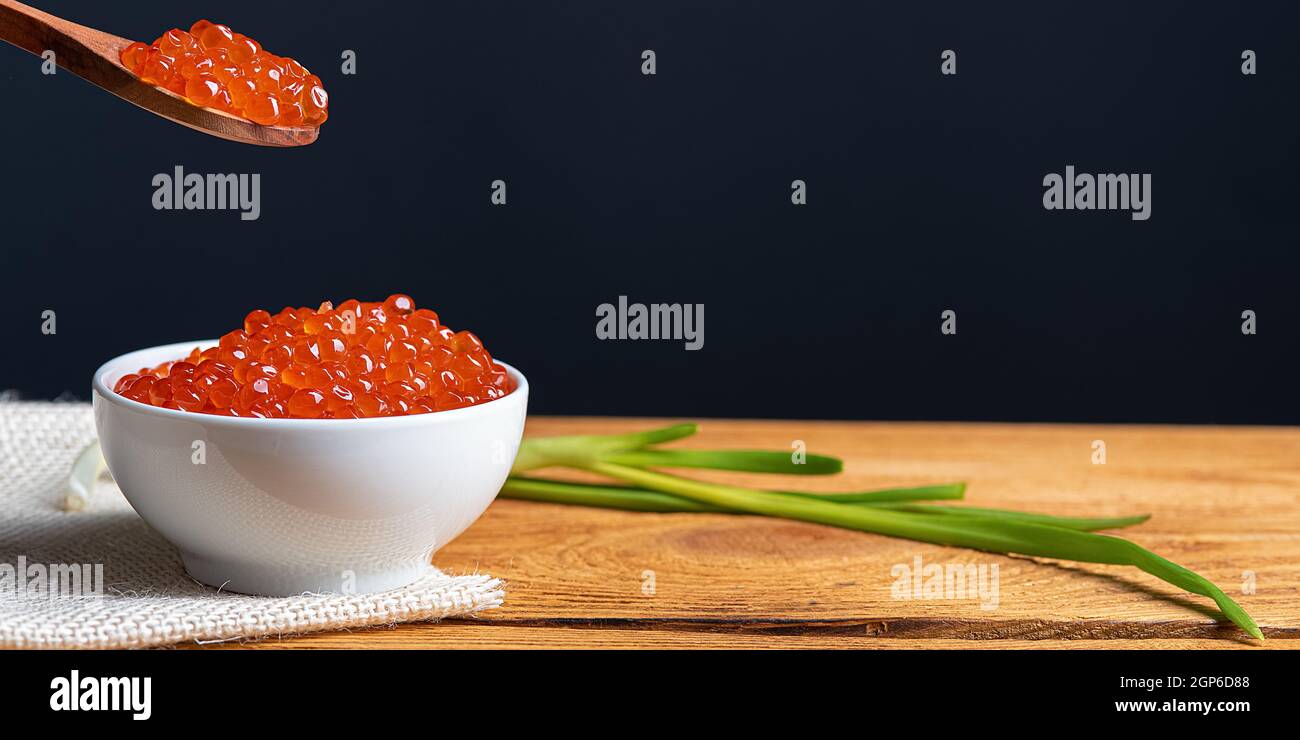 Red caviar in a wooden cup on a wooden background with a spoon. Place ...