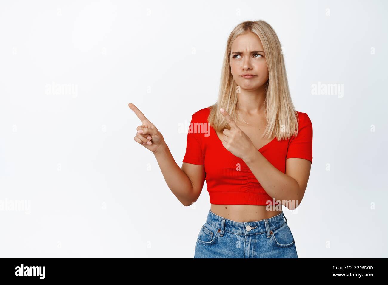 Sad grumpy blond girl pointing at upper left corner, frowning and ...
