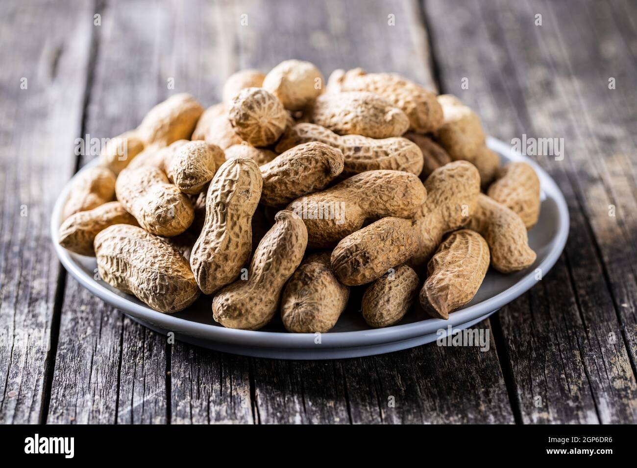 Roasted peanuts. Tasty groundnuts on plate on wooden table Stock Photo ...