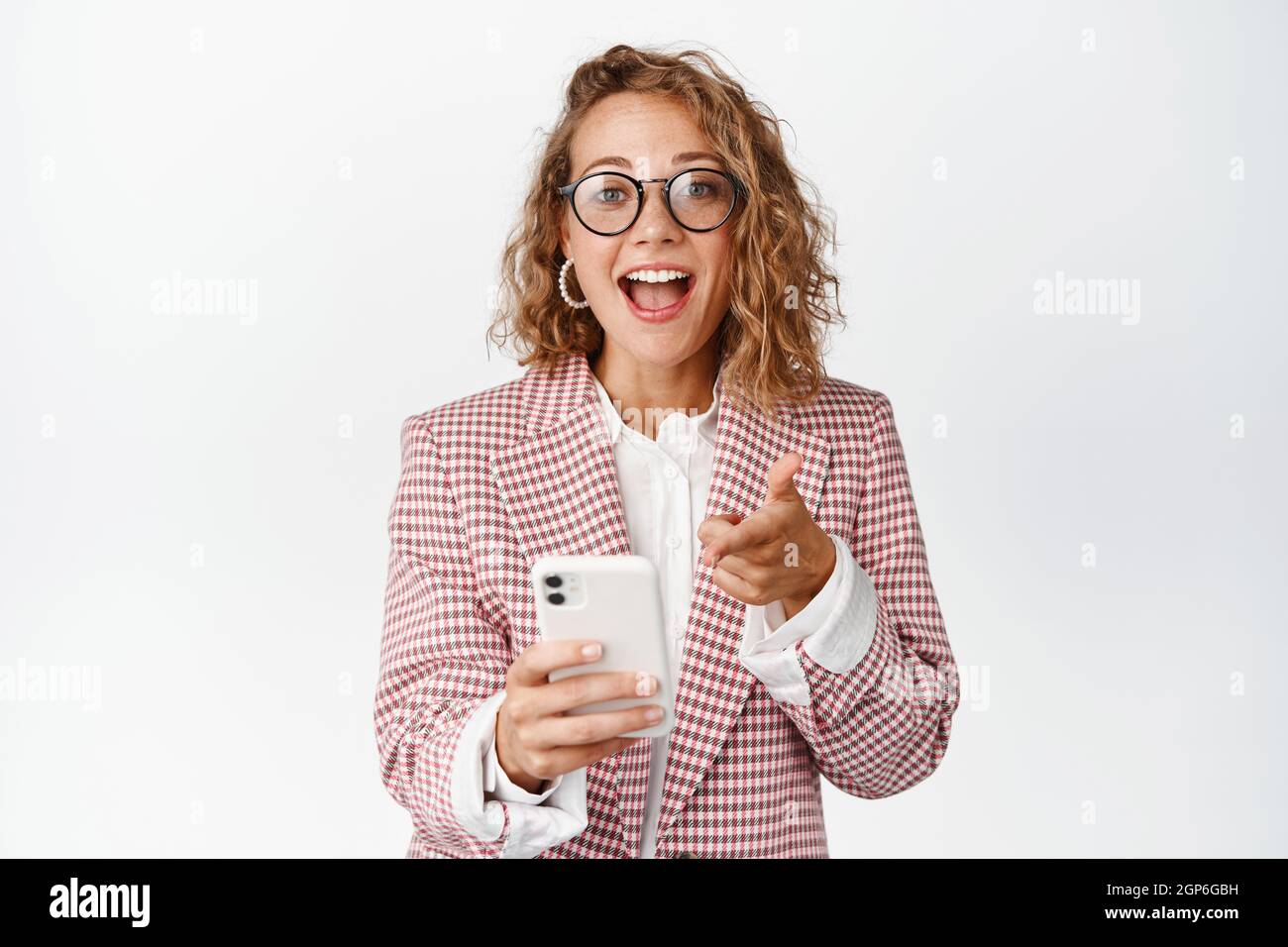Surprised business woman holding mobile phone and pointing at screen ...