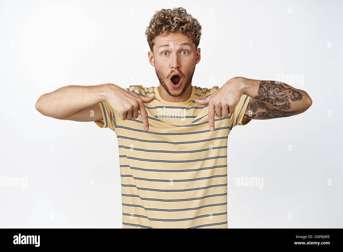 Amazed blond curly hipster guy gasping fascinated, pointing fingers ...