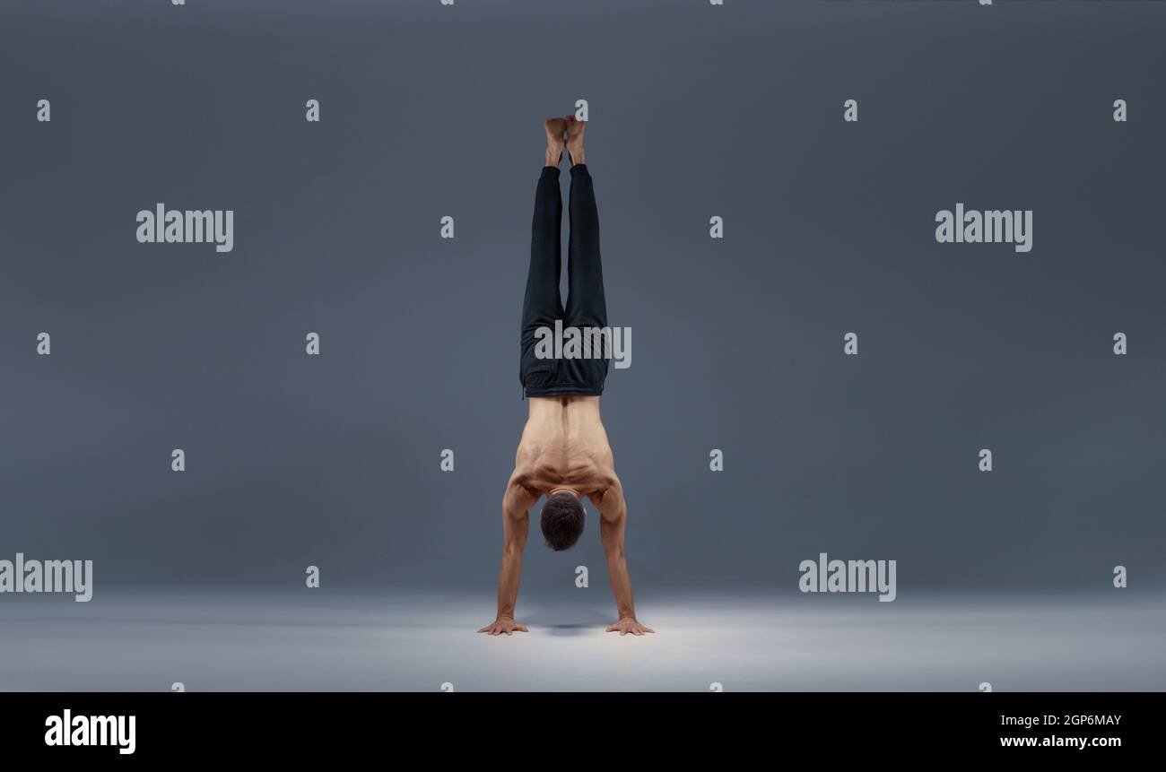 Male yoga does split on hands, back view, grey background. Strong man ...
