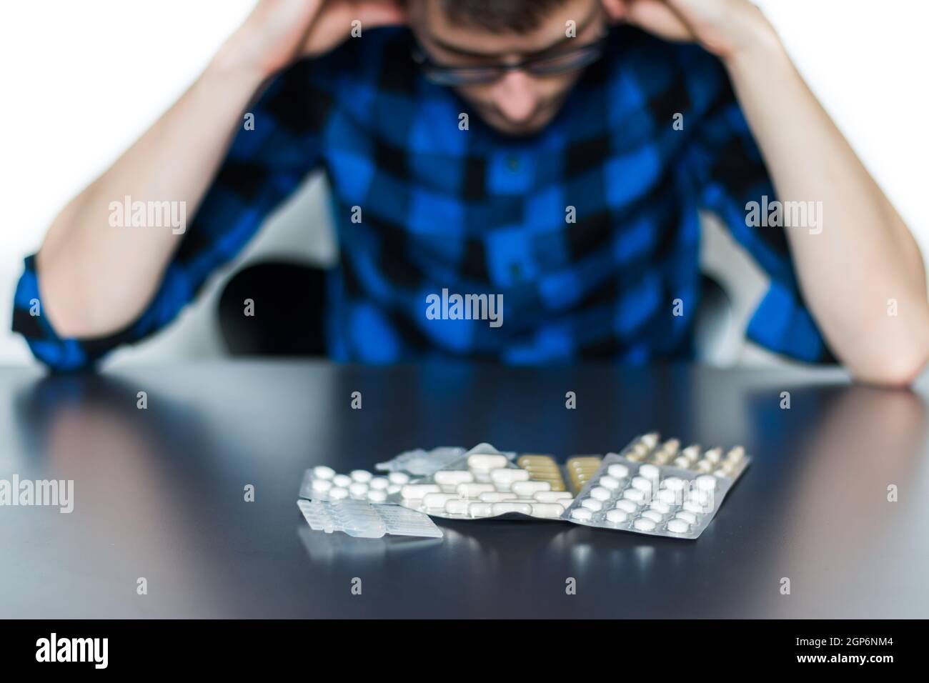 Drug abuse: Young man sitting on a table, drugs and pills in front of ...