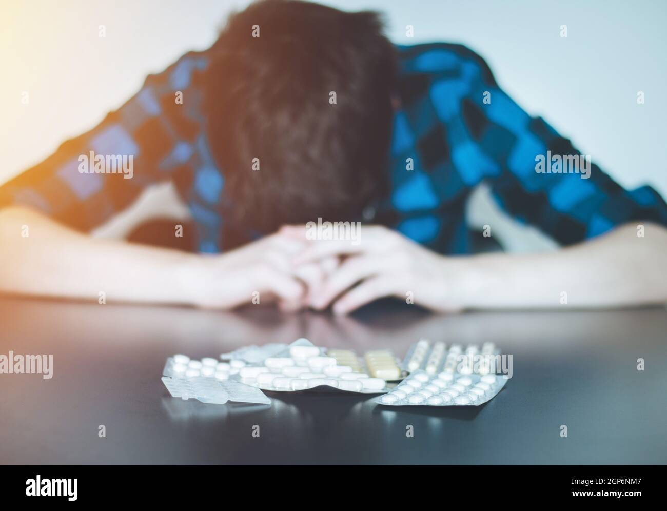 Drug abuse: Young man sitting on a table, drugs and pills in front of ...