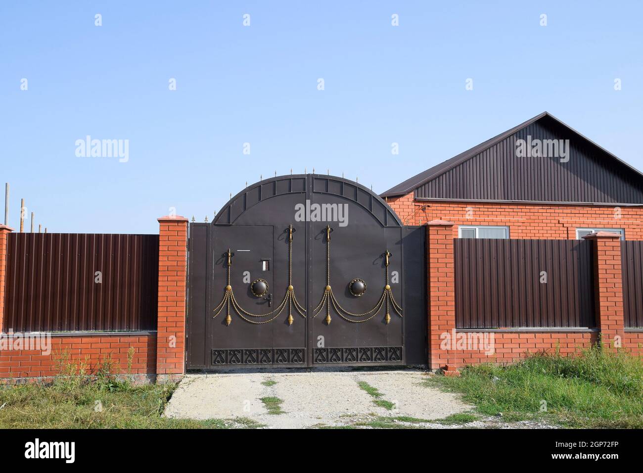 Brick house with a fence and gates. View of a new built-up fence and a ...