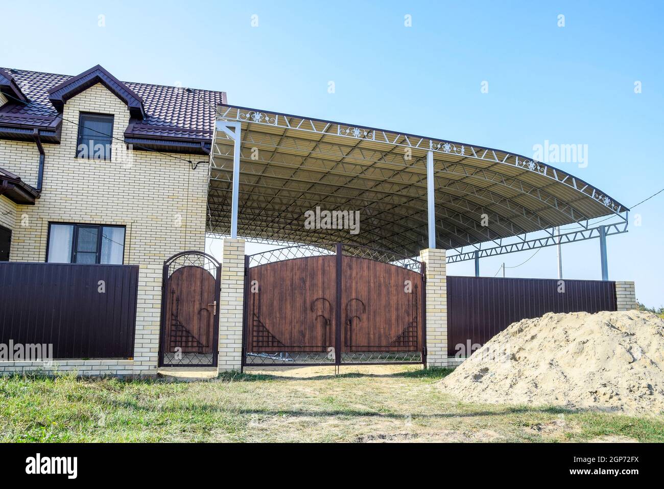 Brick house with a fence and gates. A large awning with a steel frame ...