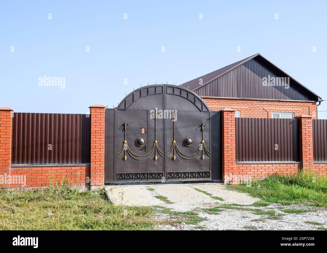 Brick house with a fence and gates. View of a new built-up fence and a ...