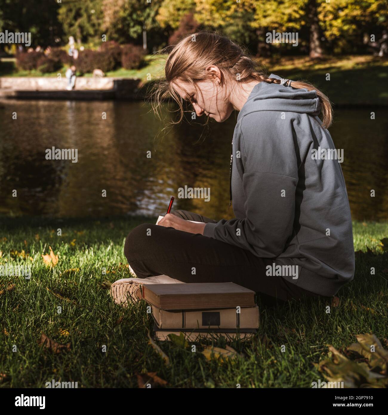 A student girl is sitting in the park on the grass and making notes. A ...