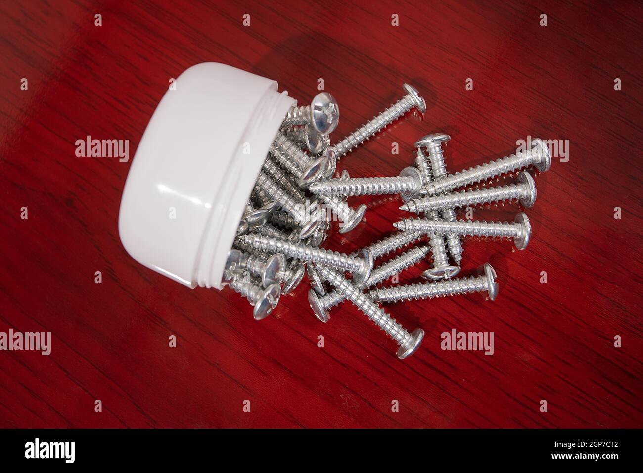A group of screws in a white bowl and on a surface with wooden finish ...