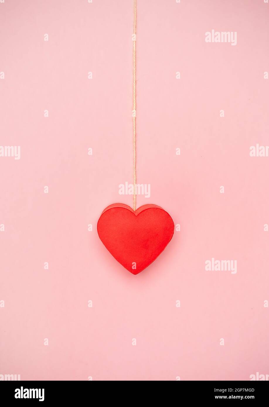 Heart hanging to a string of twine on pink background. Love concept ...