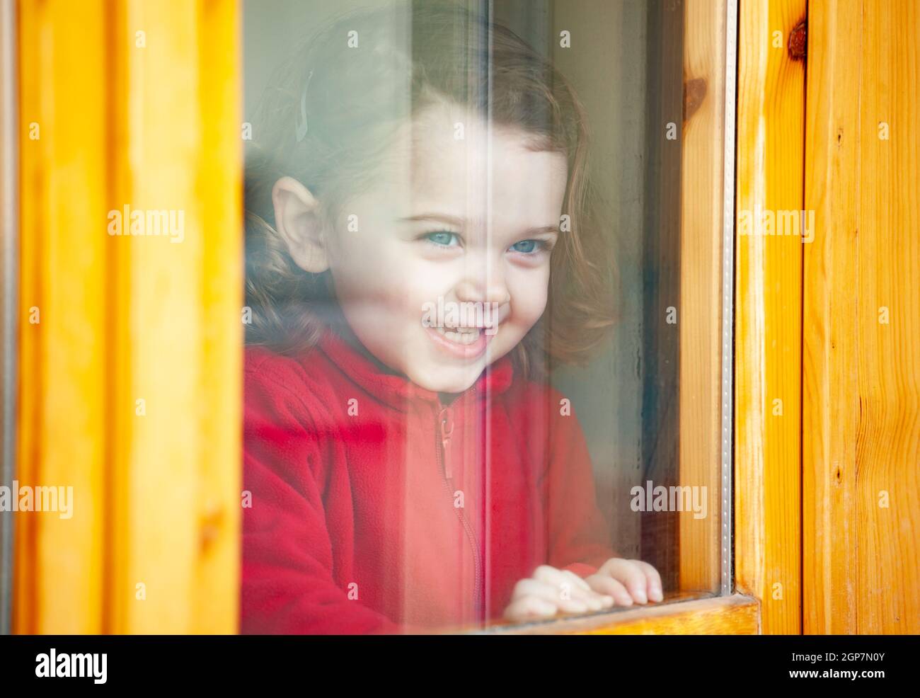 Small and lonely caucasian baby girl or toddler looking out of wooden ...