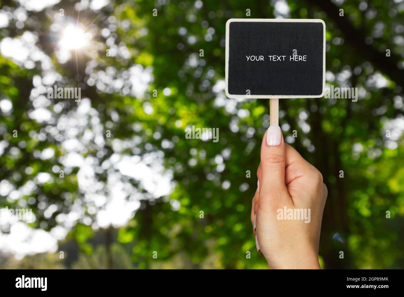 Female hand keeps sign on a background sun and foliage Stock Photo - Alamy