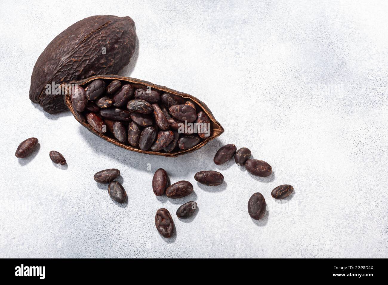 Split fermented cocoa pod with shelled cacao beans atop light grey ...