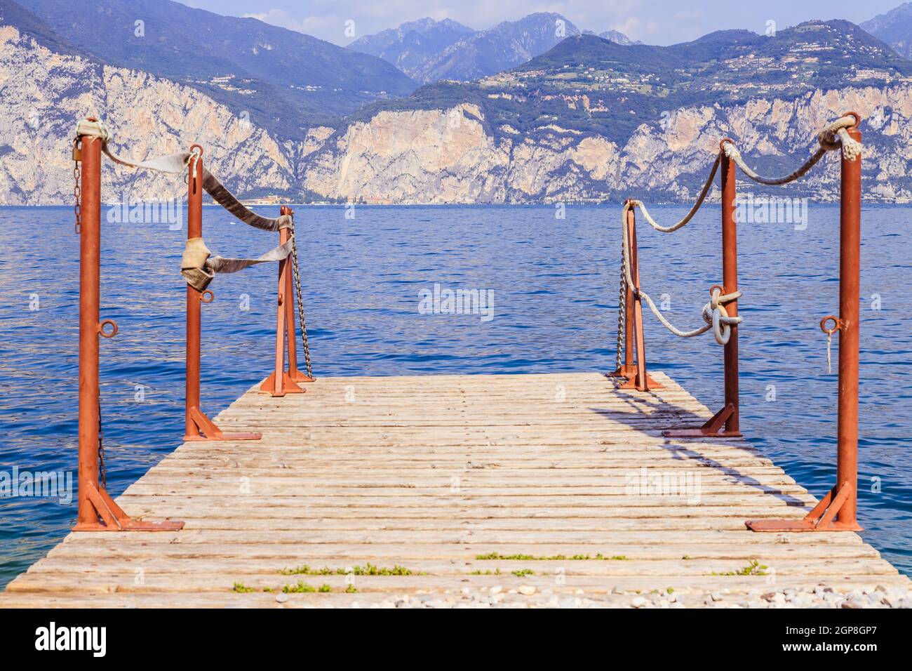 Wooden dock pier extending over blue lake water, mountains at lago di ...