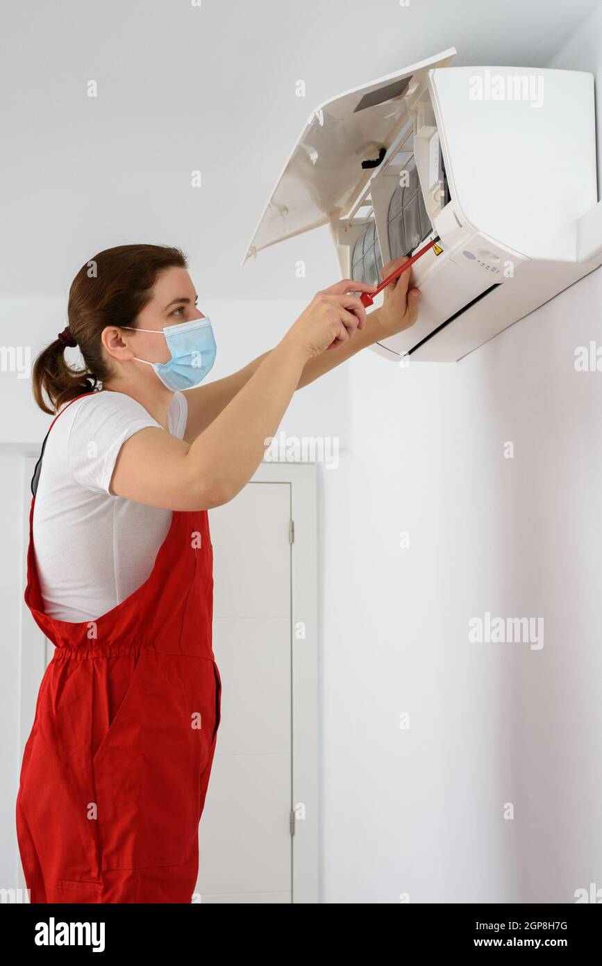 Female technician wearing face mask and repairing air conditioner ...