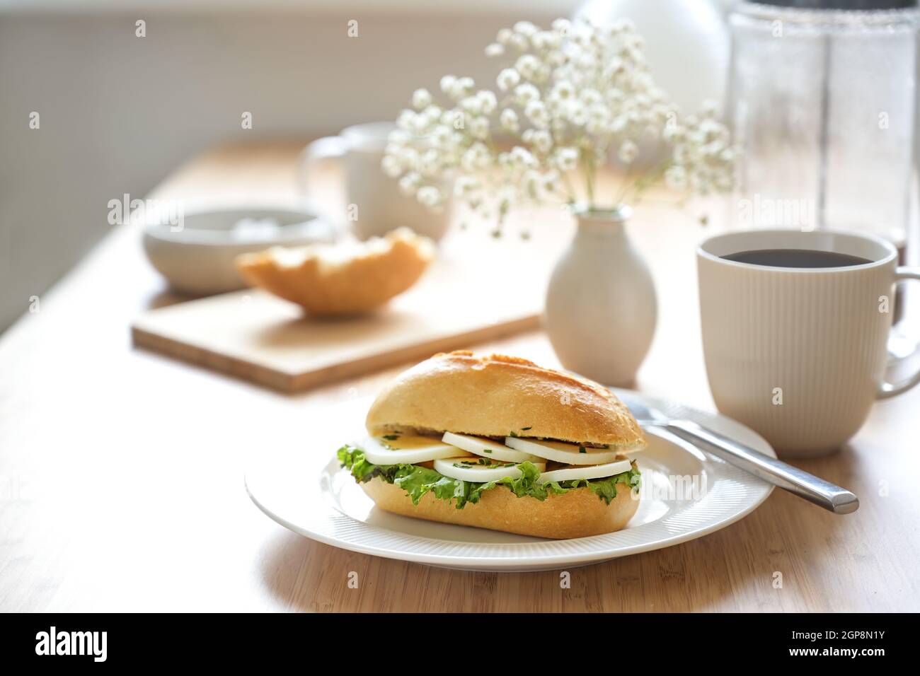 Breakfast table set with egg slices in a sandwich roll, coffee cup and ...