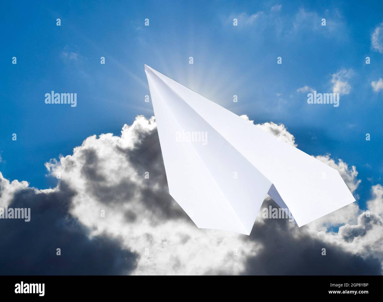 White paper airplane in a blue sky with clouds. The message symbol in ...