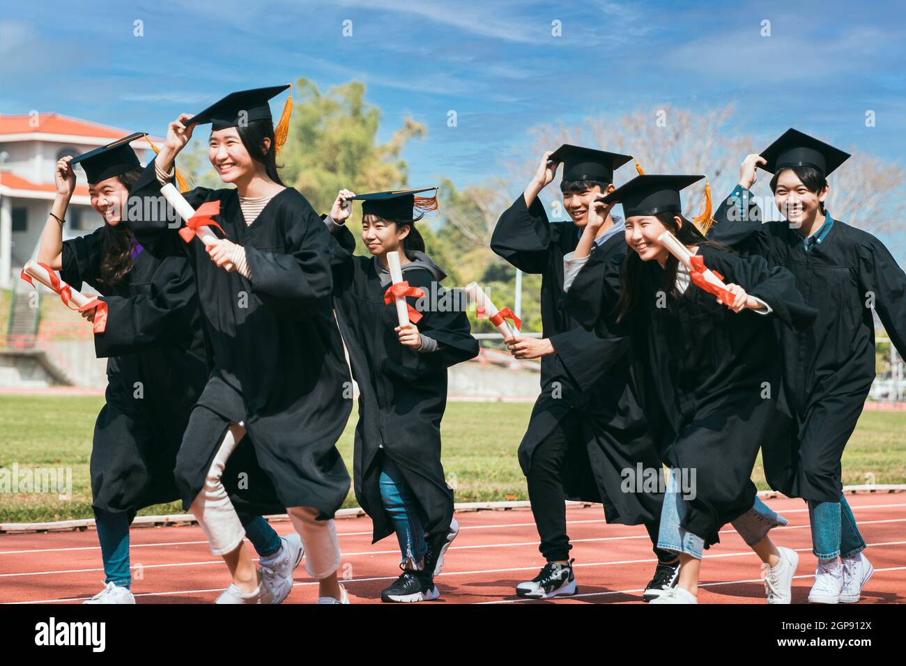 happy graduation students holding diploma and running on the stadium at ...