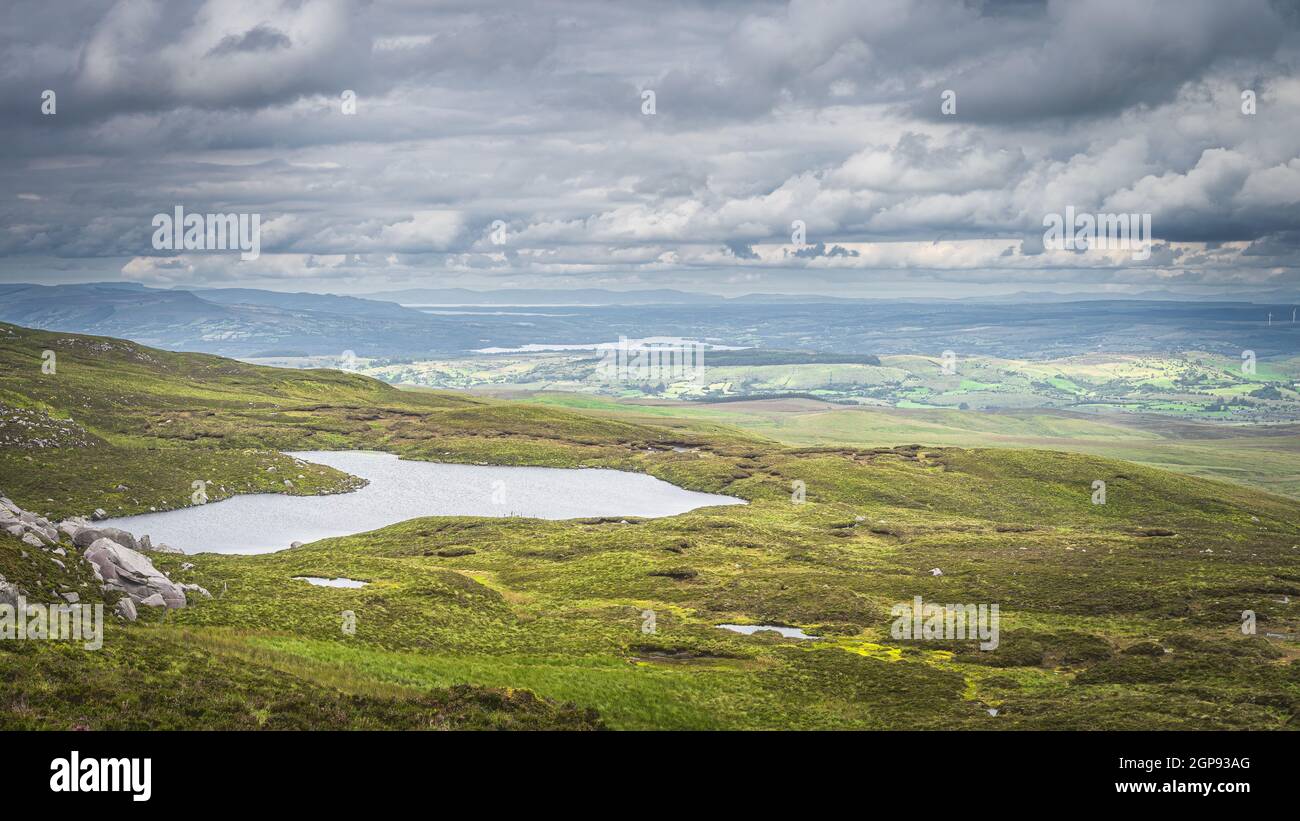 Green fields or rolling hills with small lake at footstep of Cuilcagh ...