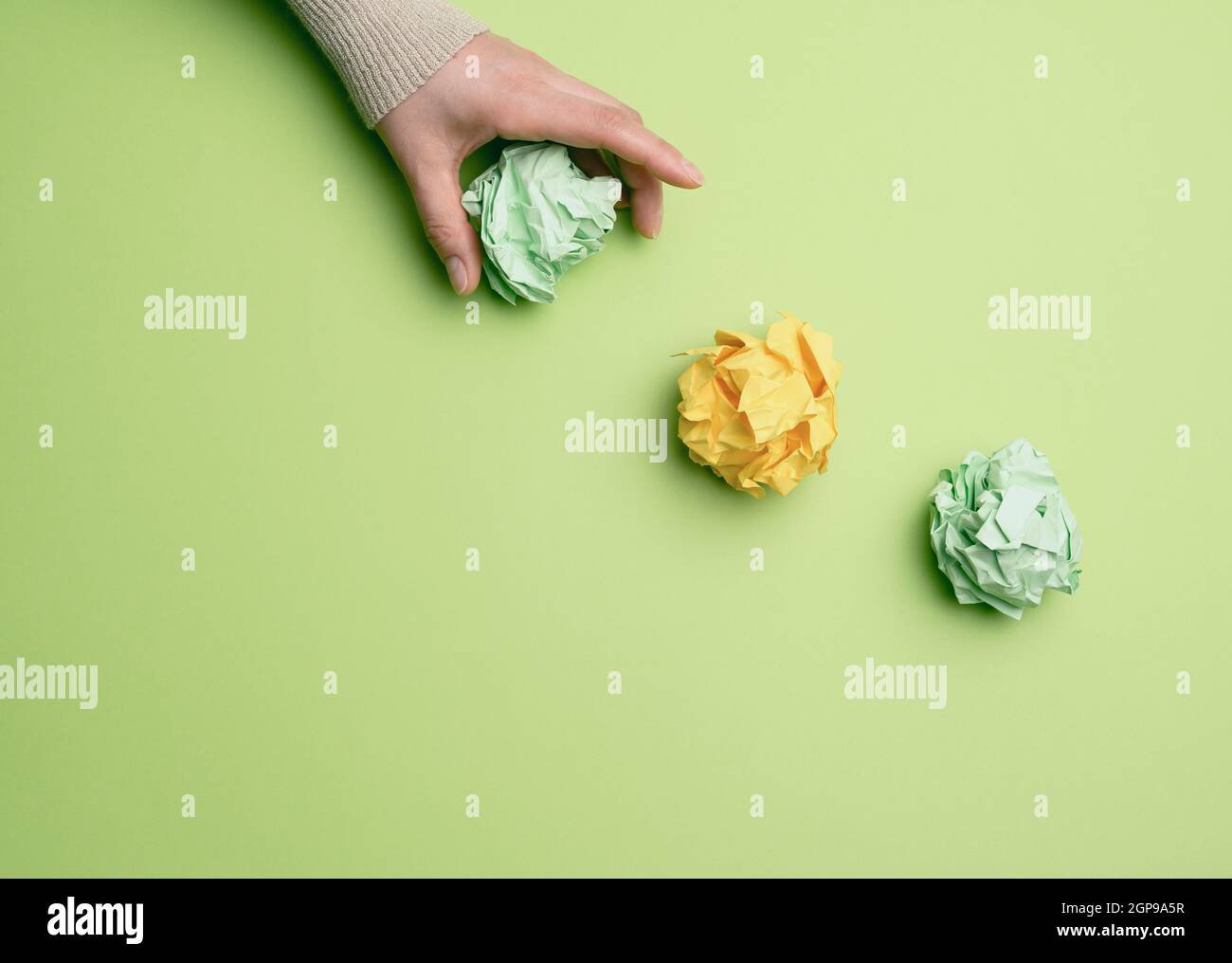 three crumpled balls of colored paper on a green background, hand ...