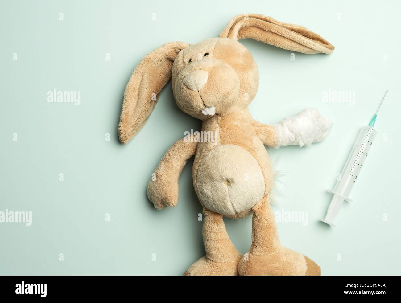 plush rabbit with bandaged paw and a plastic medical syringe on a blue ...
