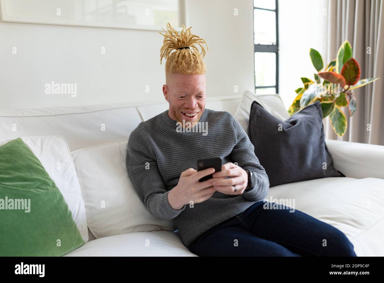 Happy albino african american man in the living room using smartphone ...